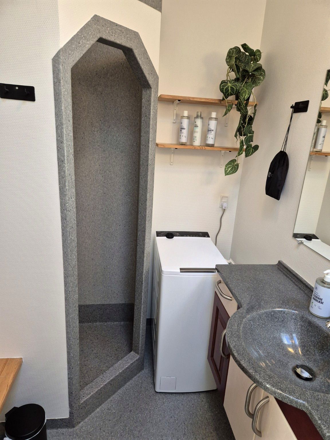Casa de banho compacta com máquina de lavar embutida, lavatório e espelho.