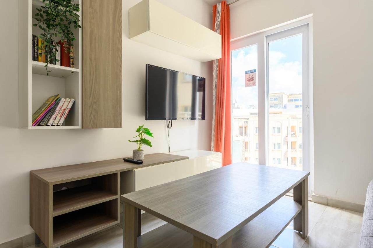 Uma sala de estar moderna com televisão de tela plana, uma mesa de madeira, uma estante de livros e um vaso com planta.
