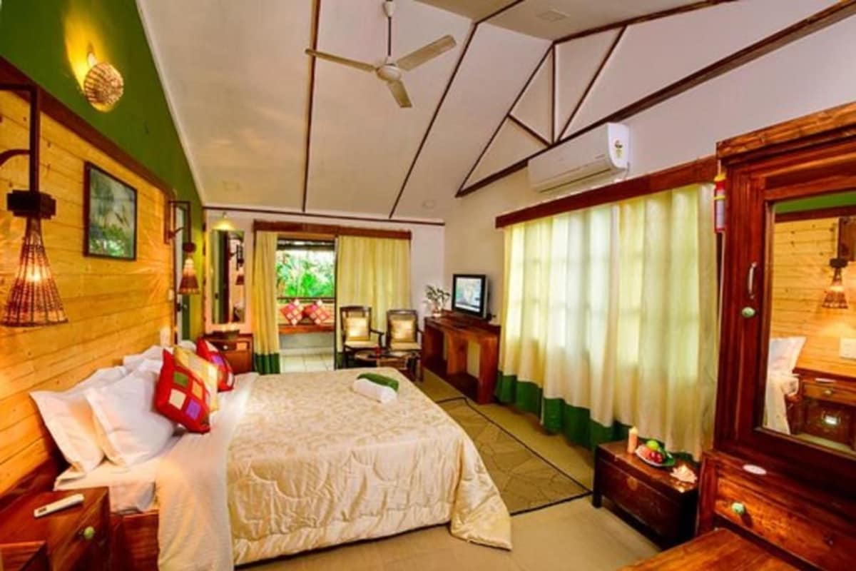 Quarto de hotel com cama, escrivaninha, cadeira, televisão e janela com cortinas.