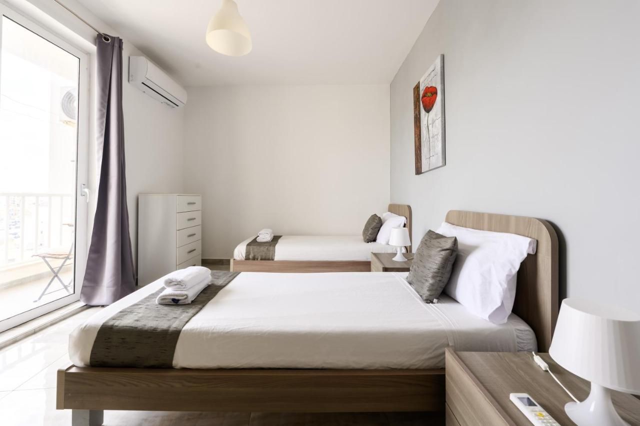 Quarto de hotel com duas camas, mesa de cabeceira com abajur, guarda-roupa e janela com cortinas.