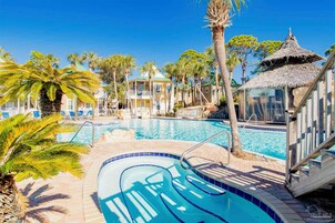 Uma piscina com terraço solar, palmeiras e uma estrutura de telhado de palha.