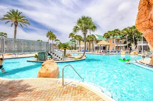 Piscina com palmeiras, espreguiçadeiras e uma formação rochosa.