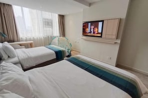 Quarto de hotel com duas camas, televisão, berço e janela com cortinas.
