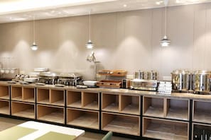 Disposição de buffet com diversos recipientes de comida e um espaço para café.