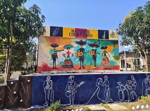 Um mural com figuras tocando instrumentos musicais tradicionais, uma placa com a inscrição 'NATURE'S COURTYARD' e um edifício ao fundo.