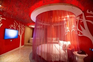 Quarto com cama de dossel, televisão e pequena mesa com abajur.