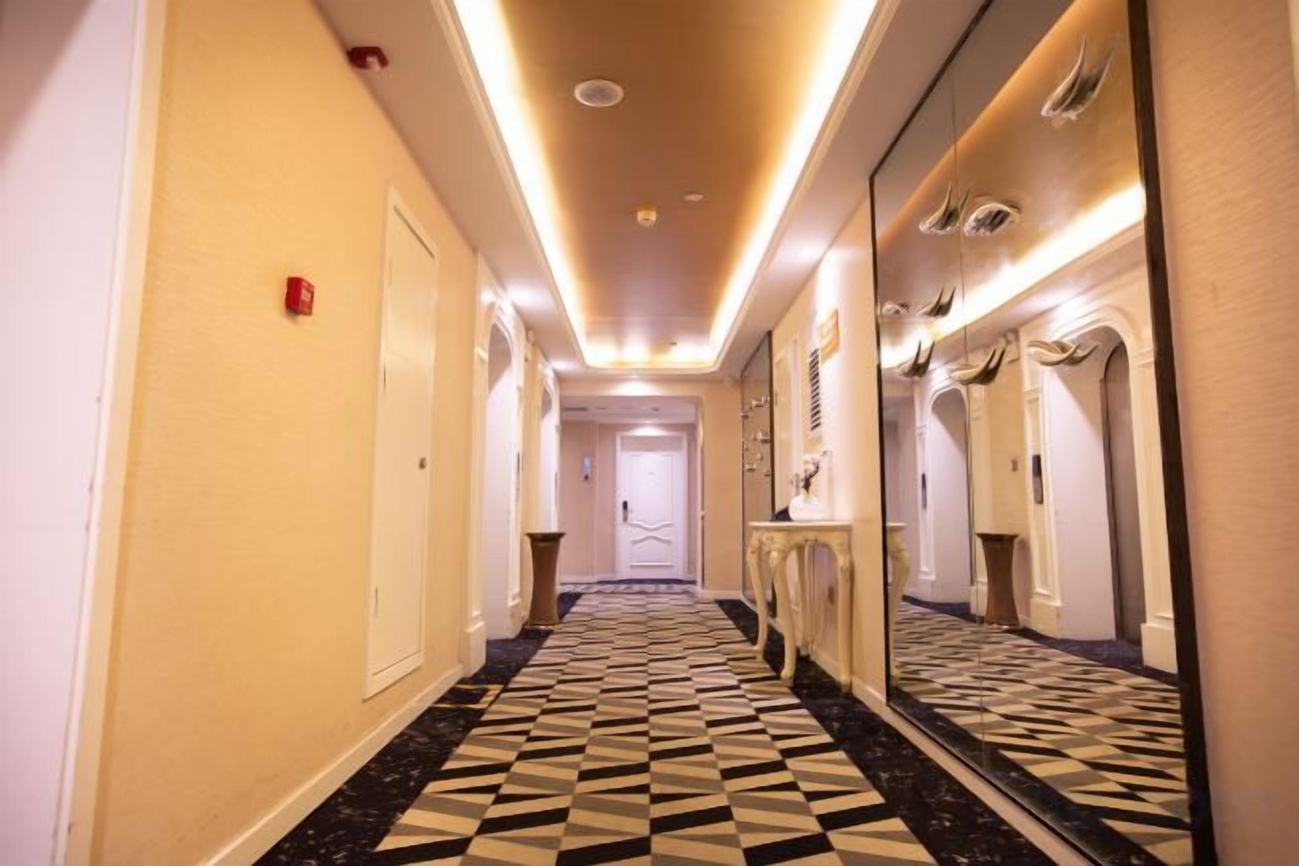 Um corredor de hotel com piso xadrez, um espelho e uma porta no final.