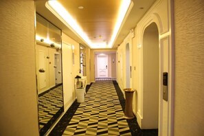 Corredor de hotel com paredes espelhadas, piso estampado e uma lixeira.