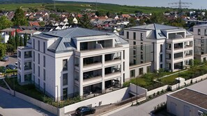 Um edifício residencial moderno de vários andares, com varandas, telhado plano e paisagem verde ao redor.