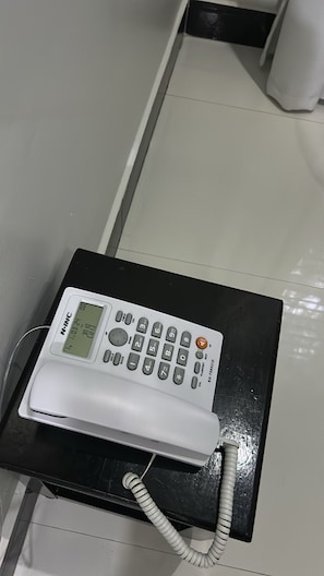 Um telefone branco sobre uma mesa preta em um quarto com chão de azulejos.