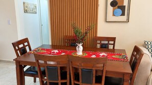 Uma sala de jantar com mesa de madeira, cadeiras e um vaso com flores.