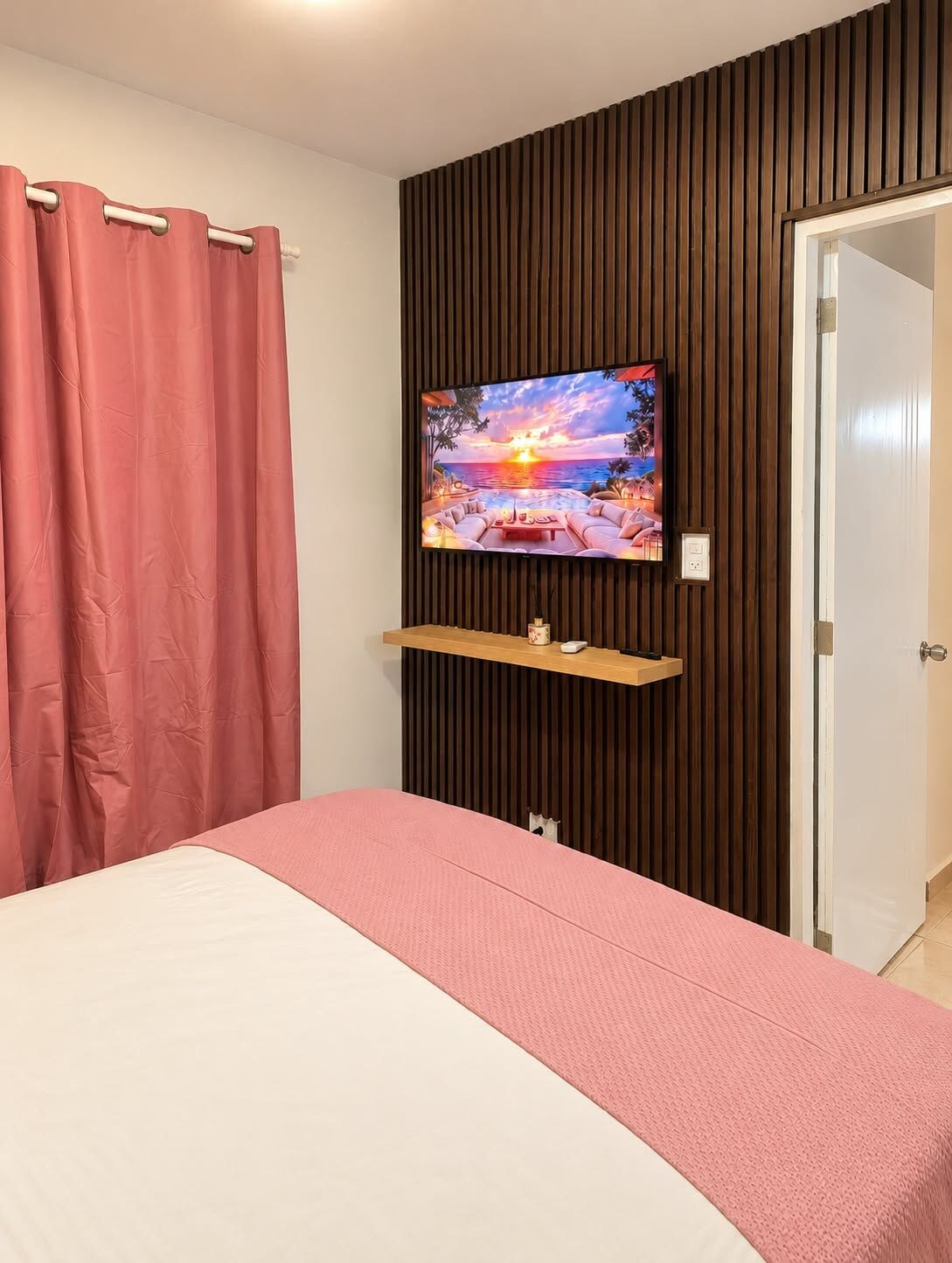 Quarto com cama, televisão fixada em parede de madeira e porta à direita.