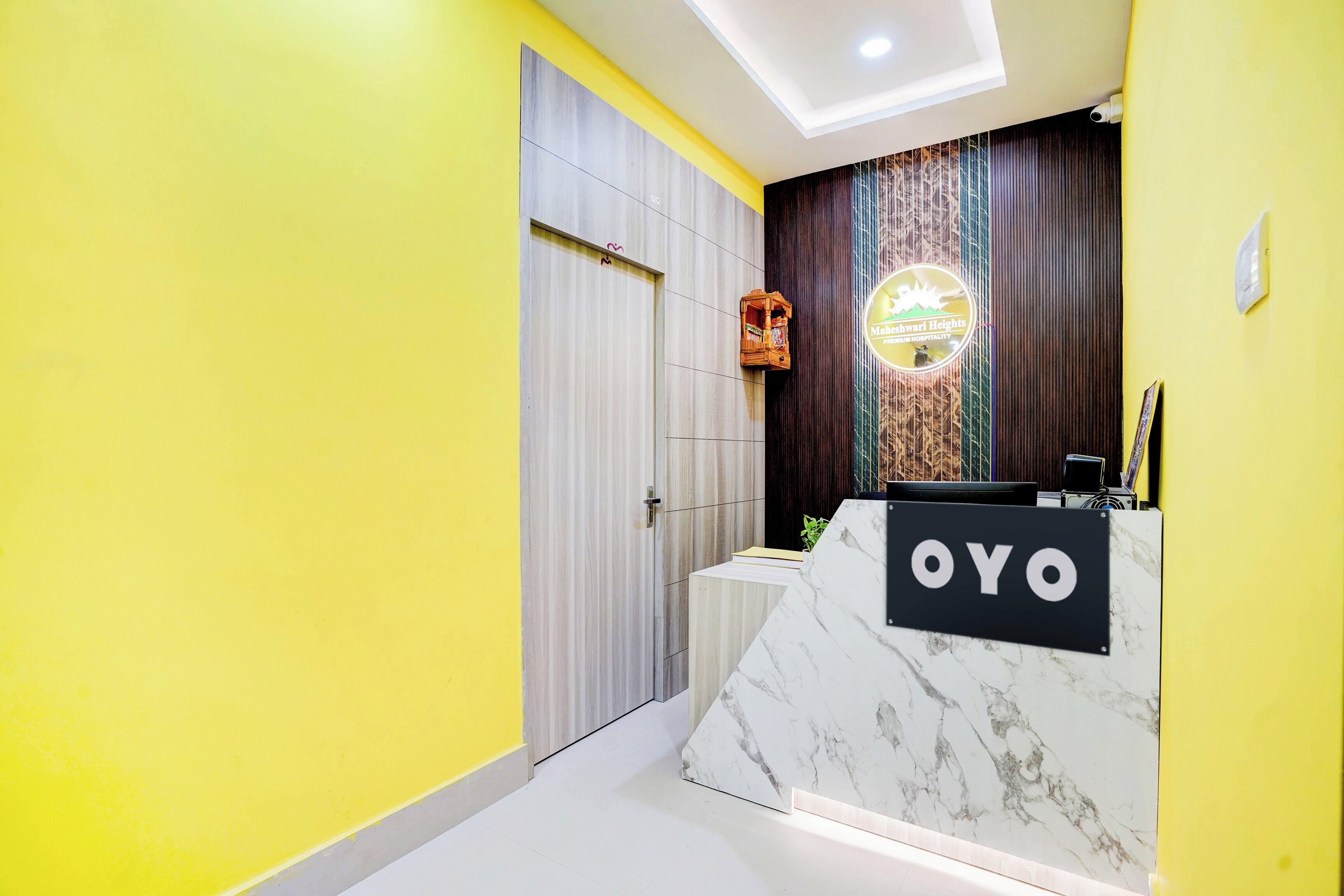 Uma área de recepção com balcão de mármore, um letreiro com a inscrição 'OYO' e uma placa na parede para 'Maheshwari Heights Premium Hospitality'.