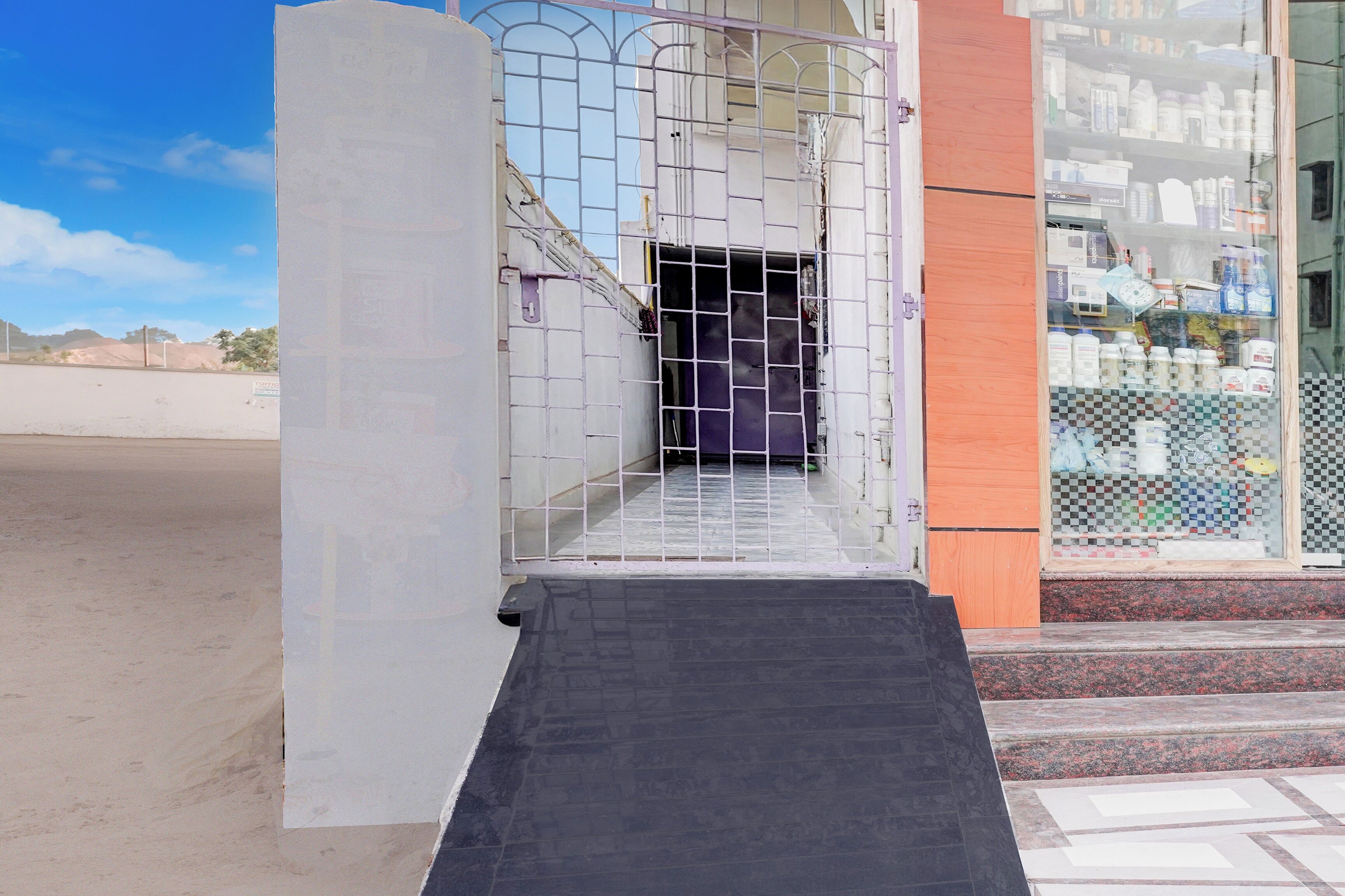 Entrada de um edifício com portão de metal, rampa de acesso à porta e vitrine com diversos artigos.