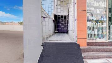 Entrada de um edifício com portão de metal, rampa de acesso à porta e vitrine com diversos artigos.