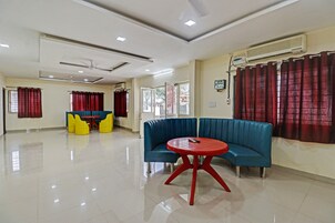 Quarto de hotel com sofá azul, mesa vermelha, cadeiras amarelas e cortina vermelha.