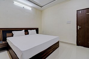 Quarto de hotel com cama, mesa de cabeceira de madeira, tomada e porta.