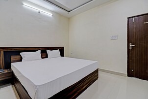 Quarto de hotel com cama, mesa de cabeceira de madeira, tomada e porta.
