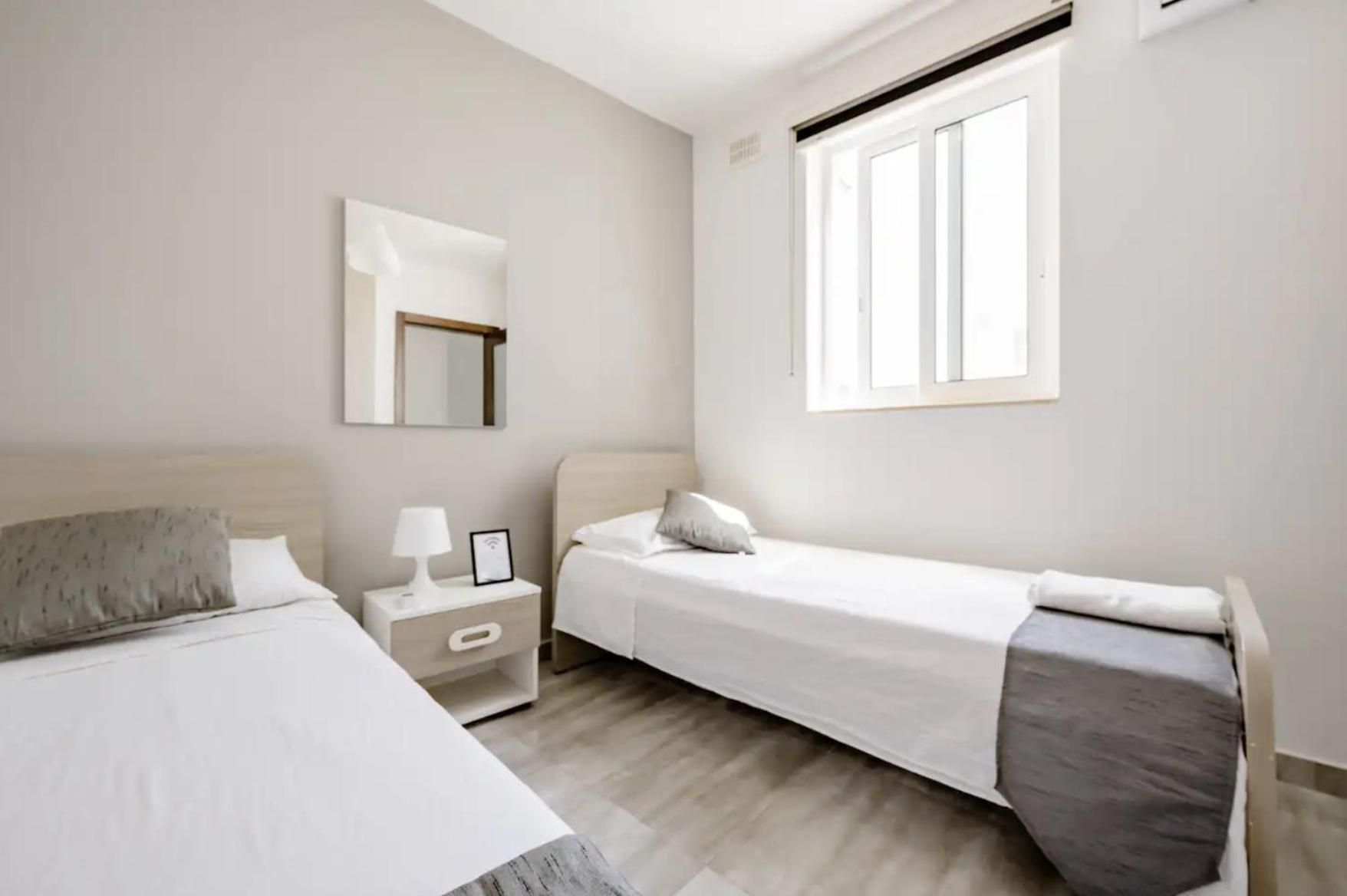 Quarto com duas camas, mesa de cabeceira com abajur, espelho e janela.