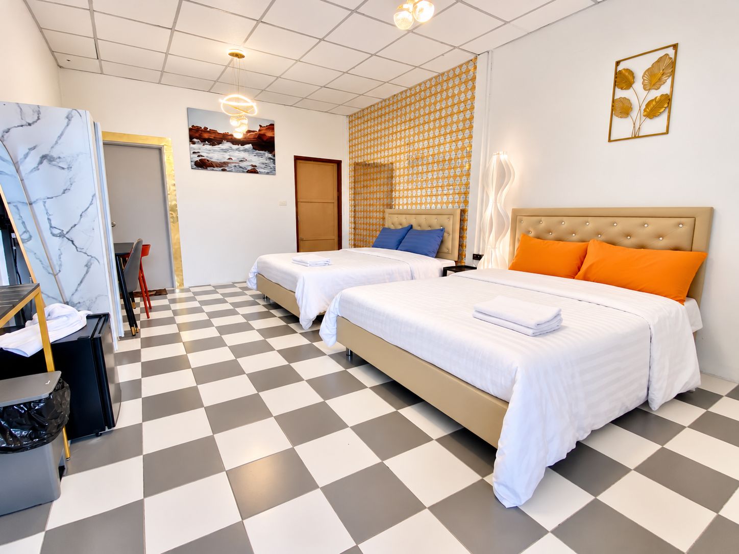 Quarto de hotel com duas camas, chão quadriculado, um espelho, uma porta e uma parede com painel decorativo.