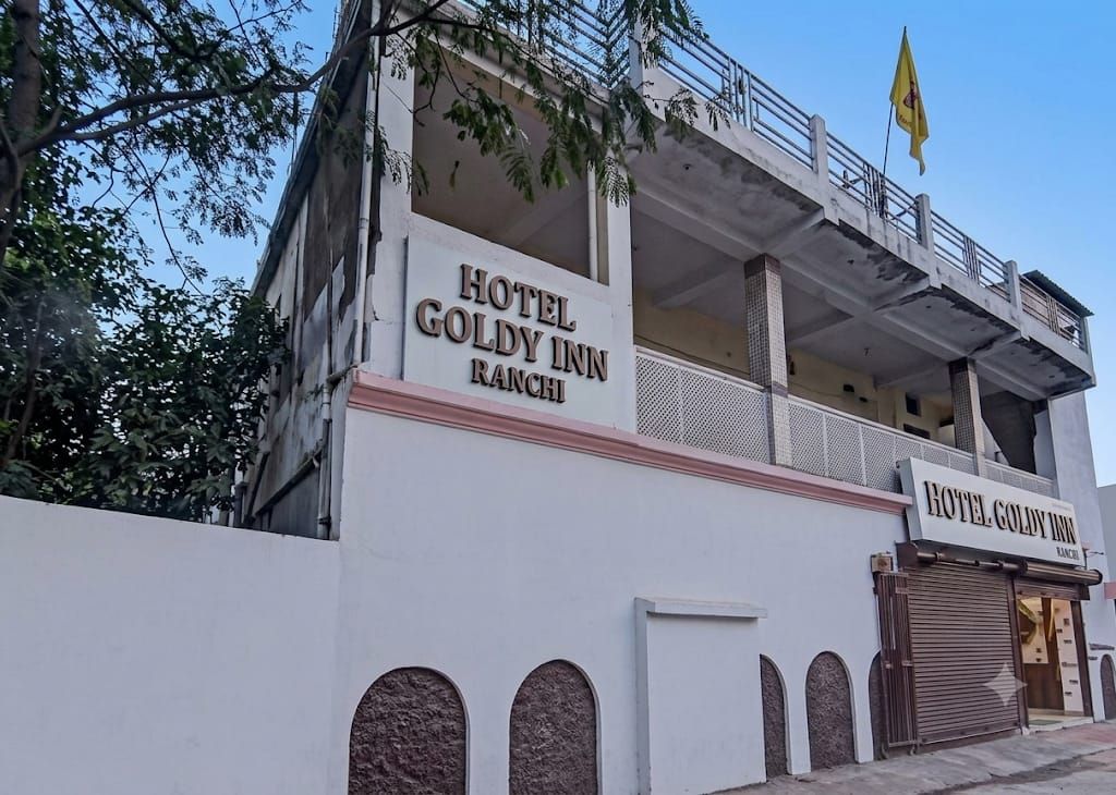 Hotel chamado 'Hotel Goldy Inn Ranchi' com uma placa, uma varanda e uma bandeira.