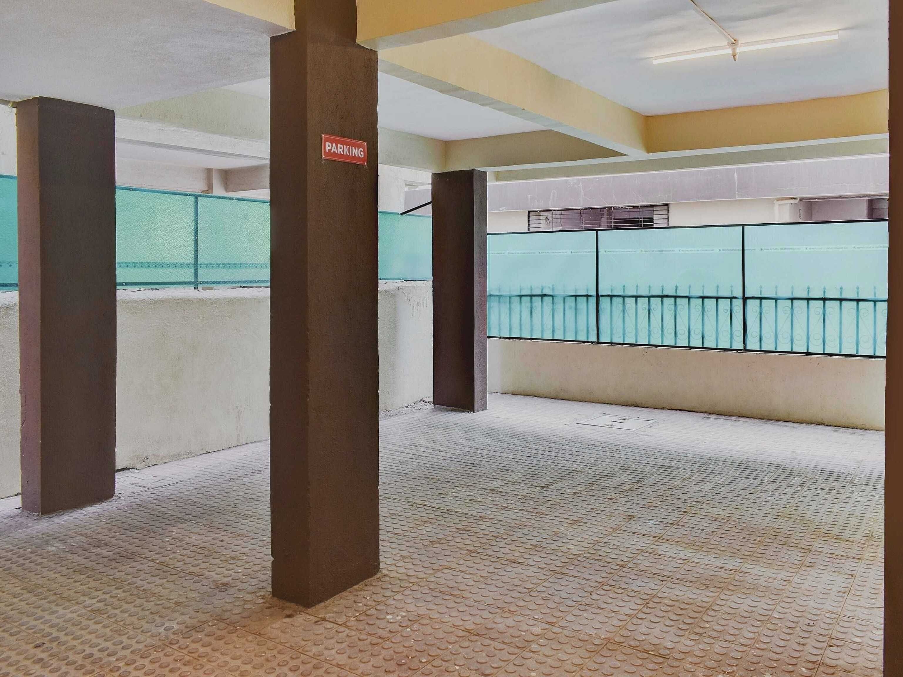 Uma área de estacionamento com placa indicando 'PARKING', pilares de concreto e piso cerâmico.