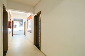 Corredor com portas em ambos os lados, um extintor de incêndio à esquerda e uma janela com persianas à direita.