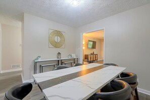 Uma sala de jantar com uma mesa comprida, cadeiras, um detalhe decorativo na parede e vista para outro ambiente.