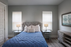 Quarto com cama, duas mesas de cabeceira com abajures, cabeceira e um quadro na parede.