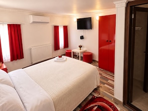 Quarto de hotel com cama grande, televisão, armário vermelho e uma pequena mesa com um vaso de flores.