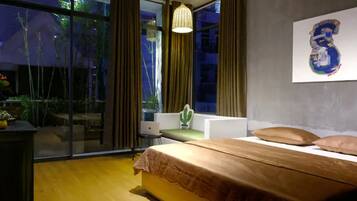Quarto com cama, escrivaninha, cadeira e uma janela grande com cortinas.