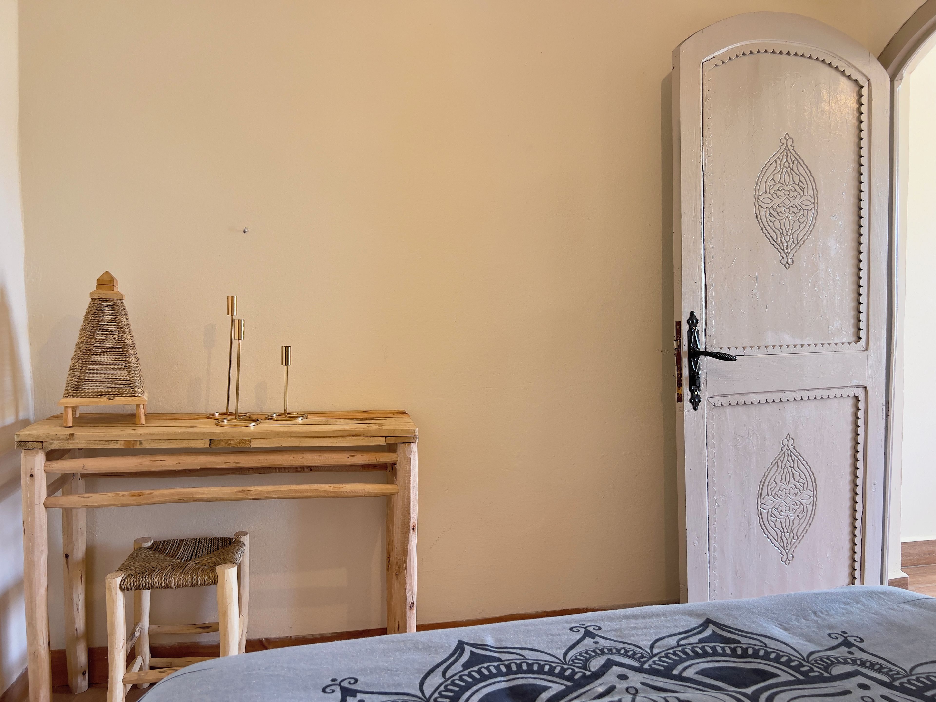 Um quarto com escrivaninha de madeira, cadeira de fibra natural e porta decorativa.
