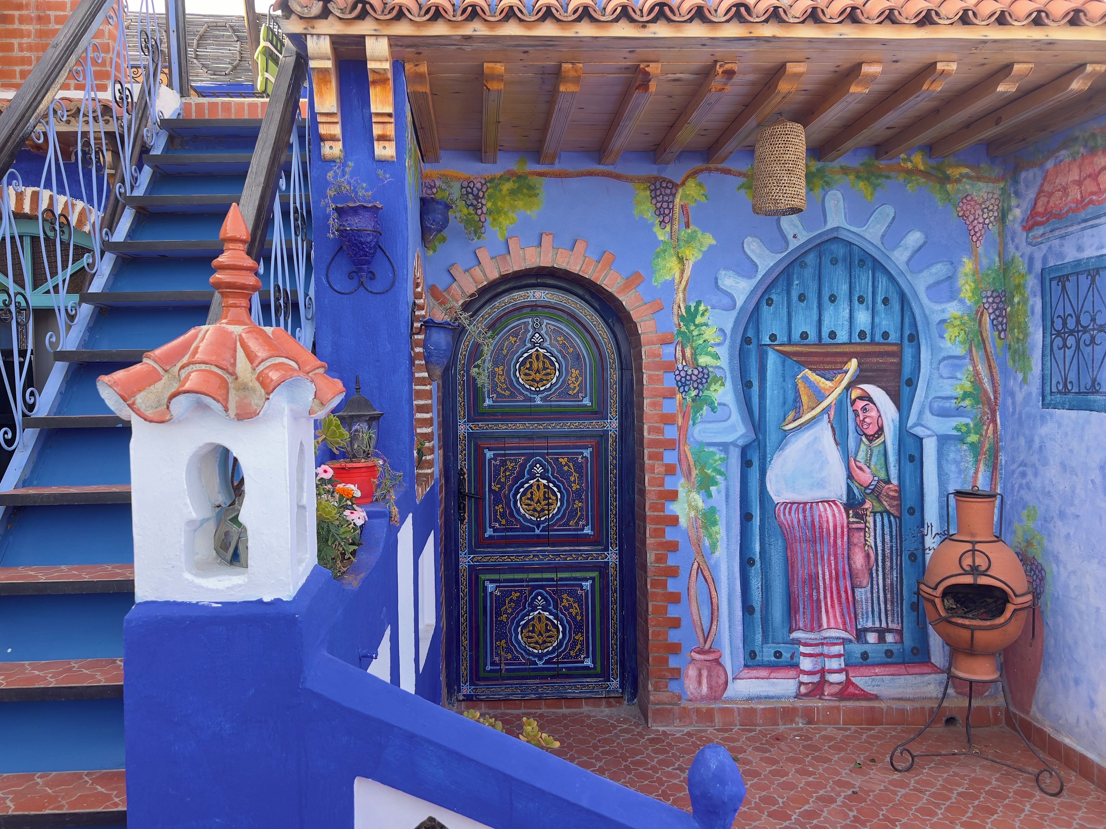 Edifício vibrante em azul e tons de terracota, com porta decorativa, escadaria e um mural de uma mulher.
