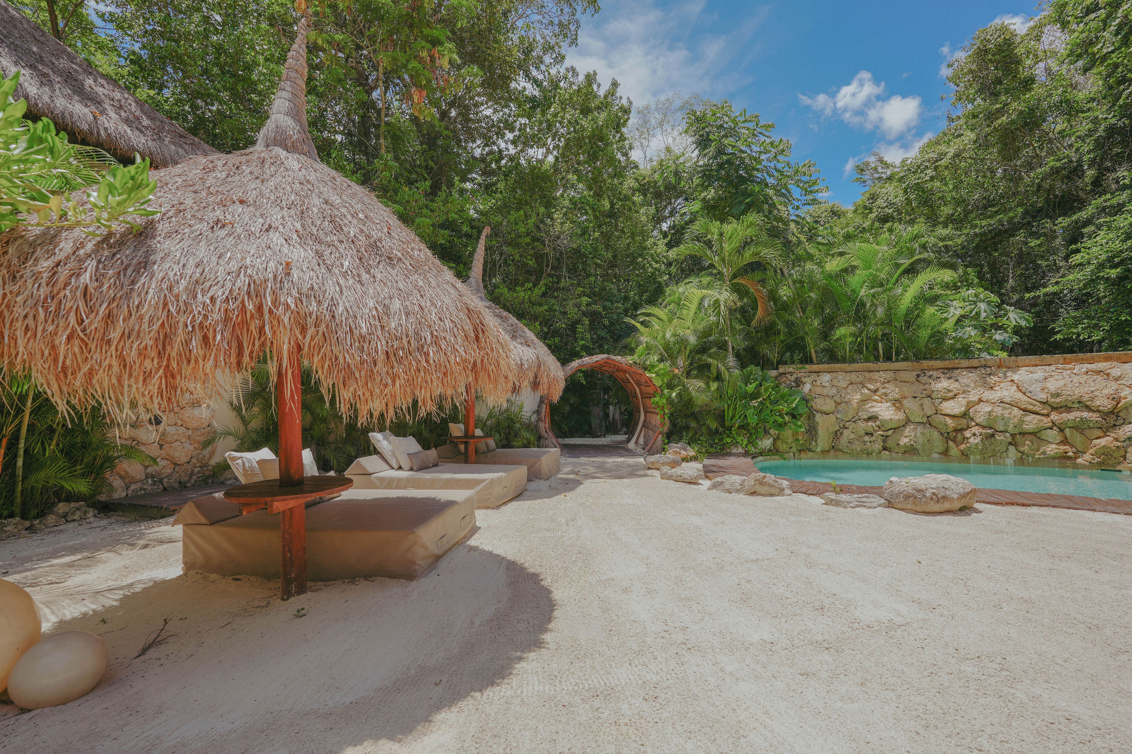 Um resort tropical com uma estrutura de telhado de palha, piscina e muro de pedra.