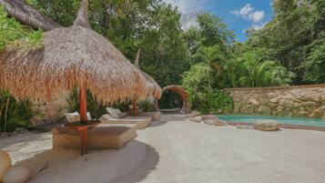Um resort tropical com uma estrutura de telhado de palha, piscina e muro de pedra.