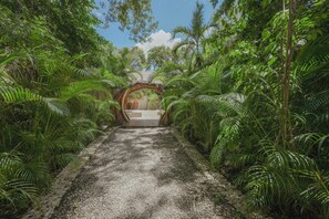 Caminho que leva a uma construção com entrada em arco, cercada por vegetação tropical exuberante.