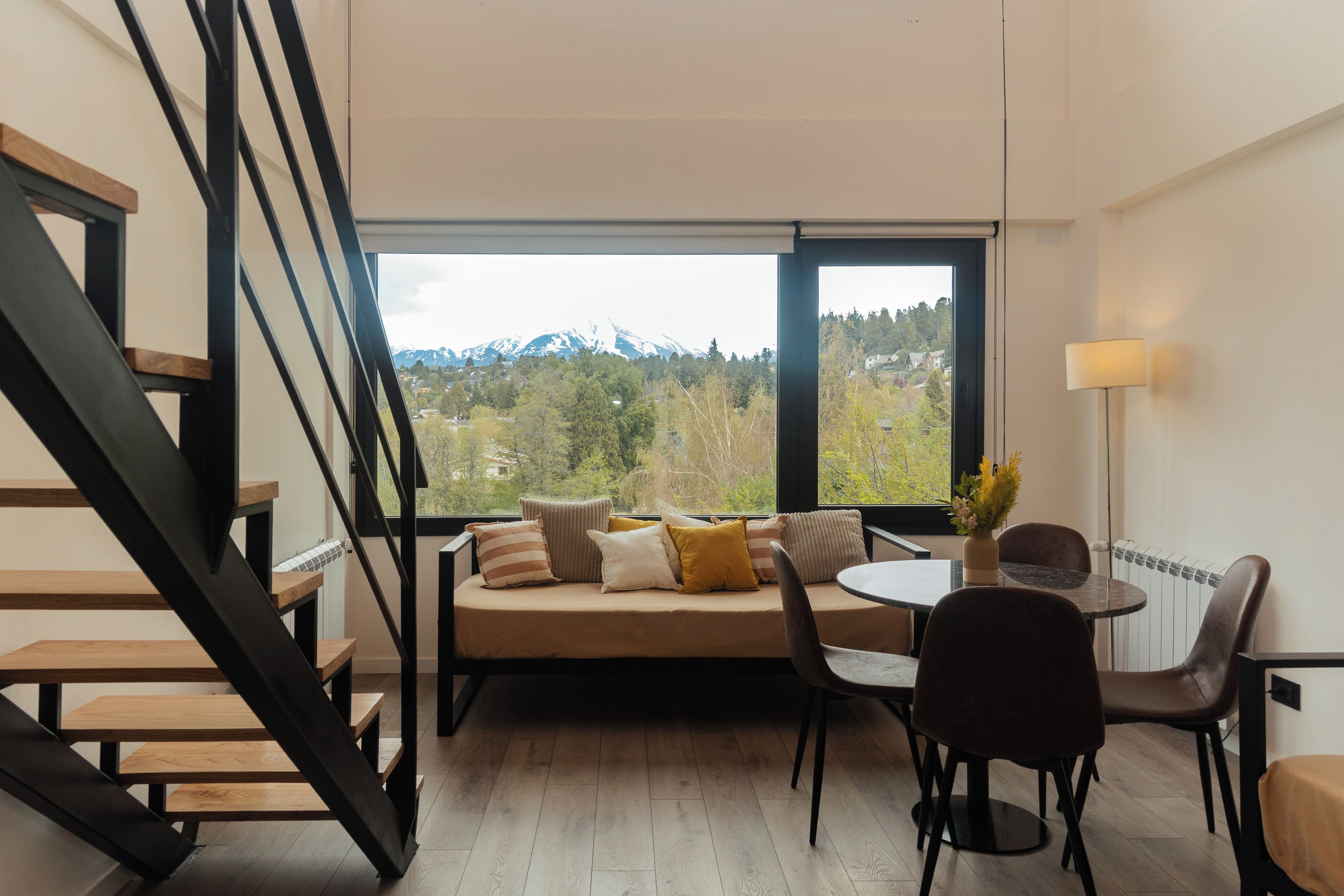 Interior moderno com sofá, mesa de jantar, cadeiras, escada e uma grande janela com vista para as montanhas.