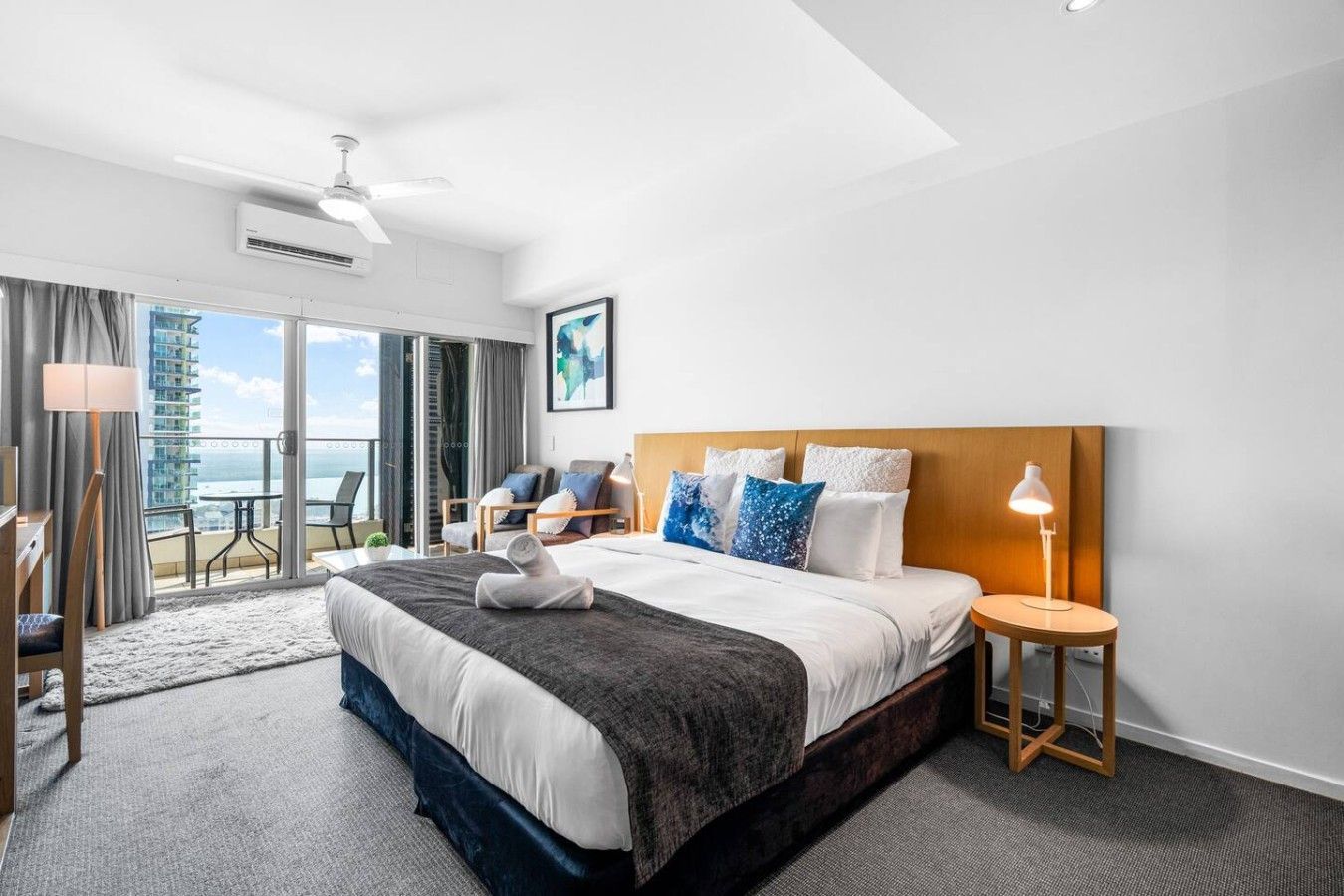 Quarto de hotel com uma cama grande, mesa de cabeceira com abajur, cadeira, varanda com vista e ventoinha no teto.
