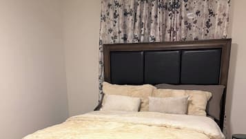 Uma cama com estrutura de madeira escura, colcha bege e cabeceira combinando.