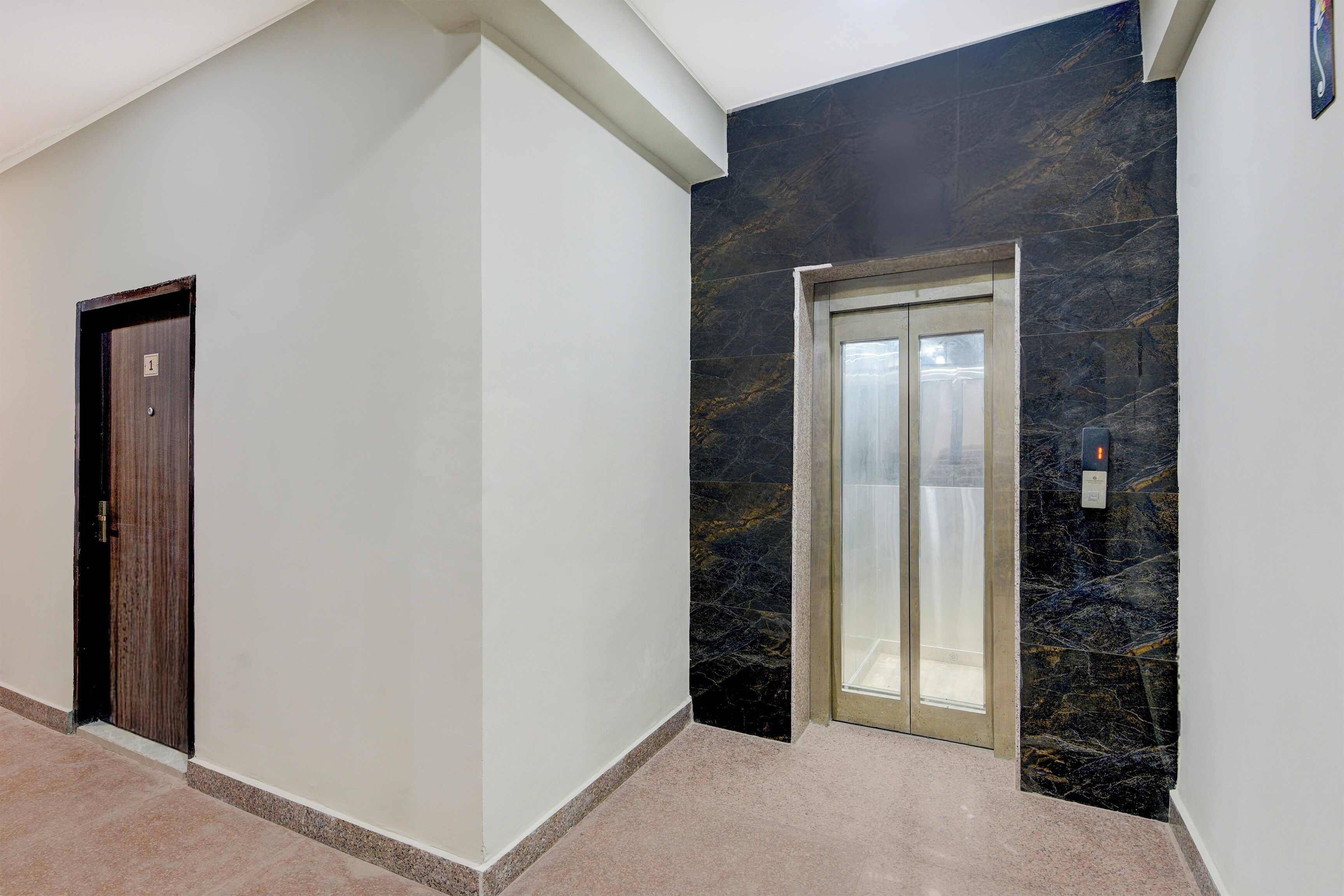 Corredor com porta de madeira marcada com o número 1, parede de mármore e um elevador com painel de controle.