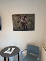 Uma fotografia emoldurada de animais selvagens na parede, uma mesa redonda pequena com um controle remoto, e uma cadeira azul.