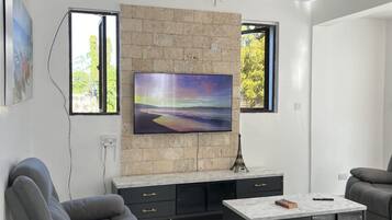 Uma sala de estar moderna com parede de destaque em pedra, televisão de tela plana, sofás cinzas e ventilador de teto.