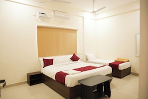 Quarto de hotel com duas camas, um ventilador de teto, um aparelho de ar condicionado e uma mesinha.