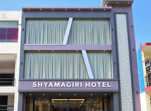 Exterior do Hotel Shyamagiri com fachada moderna, amplas janelas e um letreiro grande com o nome 'Shyamagiri Hotel'.