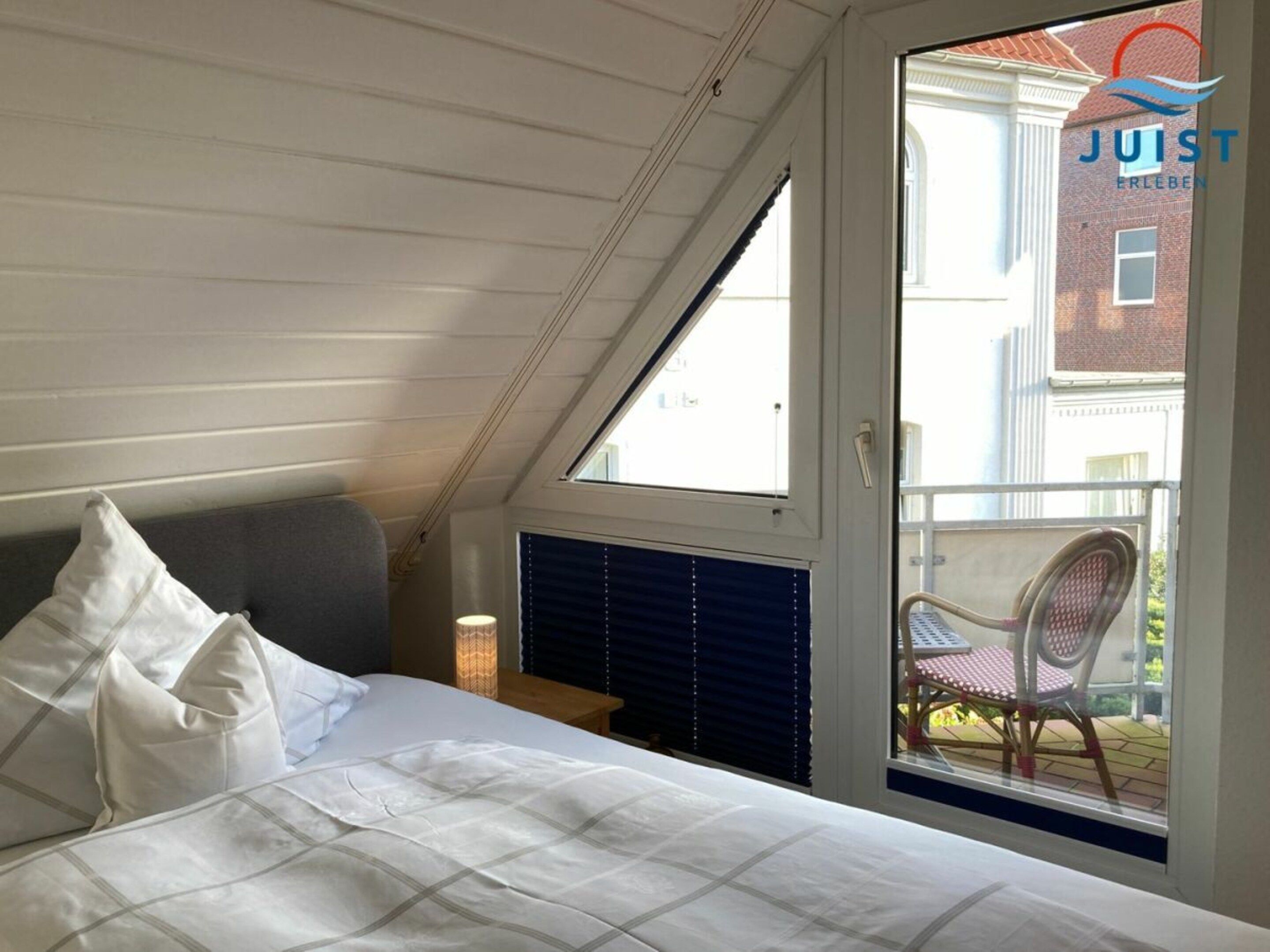 Quarto com cama, almofadas, mesa de cabeceira, abajur, janela e vista externa.