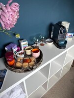 Quarto com armário branco, cesta de lanches, máquina de café e um vaso com flores.