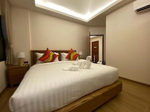 Quarto de hotel com uma cama grande, mesa de cabeceira, abajur e espelho.