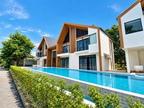 Um edifício residencial moderno com piscina, grandes janelas e um jardim bem cuidado.