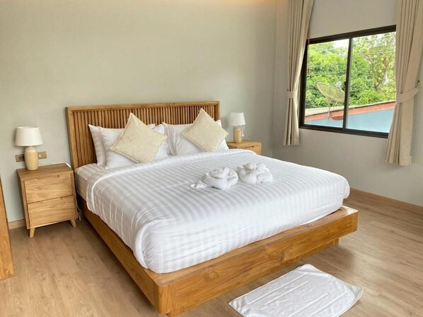 Quarto com estrutura de cama de madeira, roupa de cama branca, duas mesas de cabeceira com abajures e uma janela com vista para o verde.