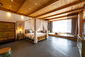 Quarto com cama de dossel, teto de madeira, parede de tijolos e janela com cortinas.